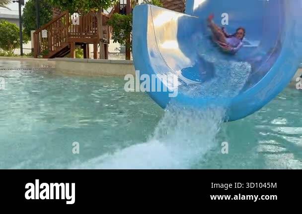 Kid wearing goggles sliding fast into a pool making splash and laughter ...