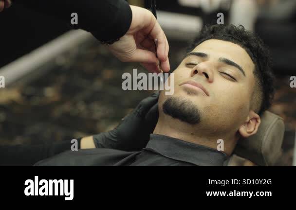Professional barber using a straight razor to style and shape a young ...
