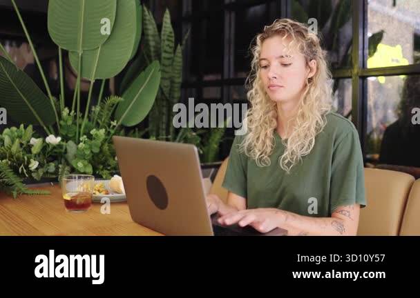 Young woman with curly blonde hair working on her laptop computer ...