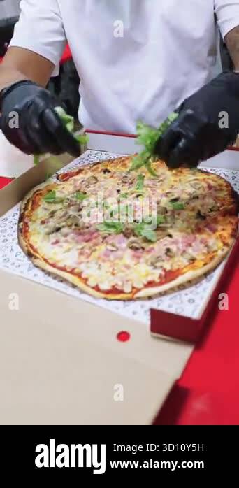 Close up of a pizzeria chef wearing black gloves carefully placing ...