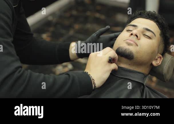 Professional hairdresser shaving a relaxed male clients beard in a ...