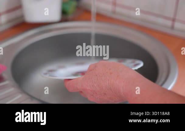 Womans hands are seen washing a decorative plate with dish soap under ...