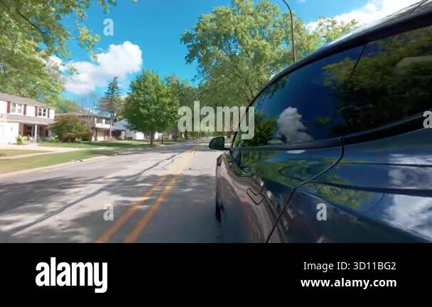 A car driving along the residential street on bright sunny day, with ...