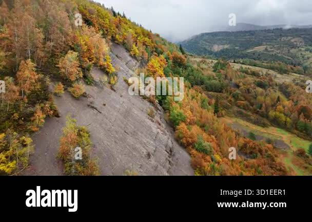 An aerial shot of a steep, rocky slope covered in trees in various ...