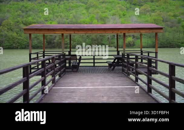 Wooden pier and covered seating area extending over tranquil lake. Lush ...