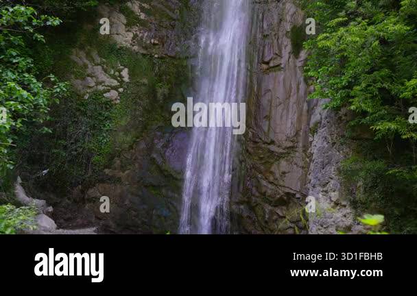 Beautiful small waterfall cascading down rocky cliff face. Lush forest ...