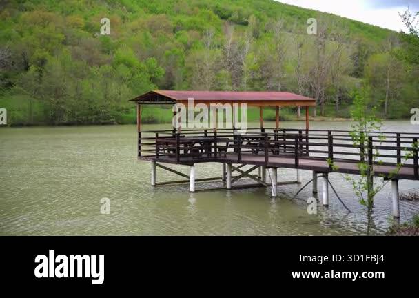 Wooden pier and covered seating area extending over tranquil lake. Lush ...