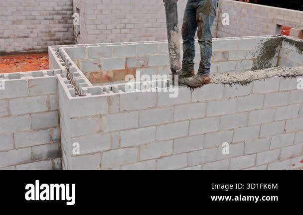 Construction worker pours concrete while laying blocks for new home ...