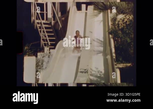 Eight year old girl sliding down a water slide and joyfully splashing ...