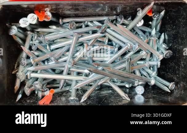 4K close-up of silver steel nails stacked in black box, sharp metallic ...