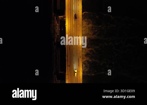 Cars drive along illuminated dam at night, showcasing dynamic motion ...