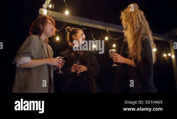 Friends enjoying drinks and conversation on a patio at night. The warm ...
