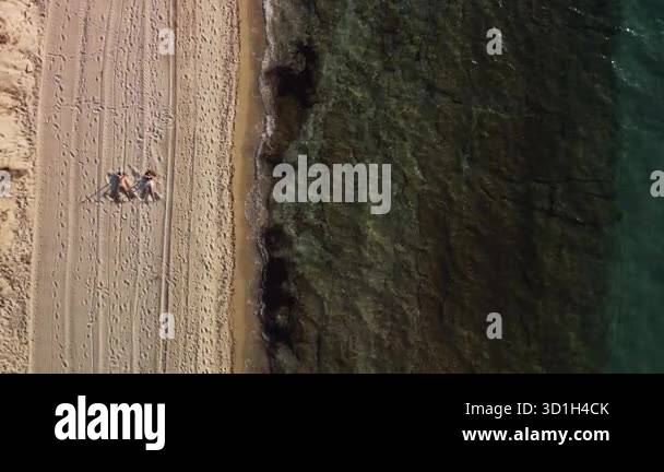 Two friends make sand angels on a sunny beach next to the ocean. Aerial ...