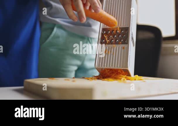 Close up of a person grating a fresh orange carrot on a wooden cutting ...