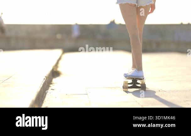 Back view of a young woman skateboarding on a sunny day at a concrete ...
