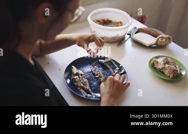 Close up of a womans hands meticulously deboning cooked fish on a blue ...