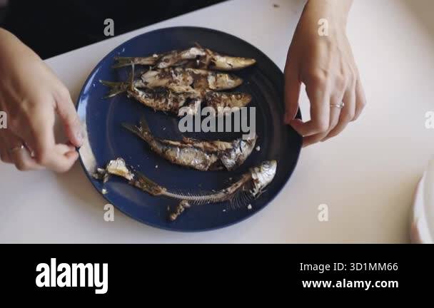 Womans hands meticulously deboning small grilled fish on a dark blue ...