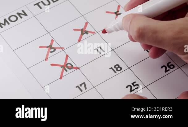 Close-up image of a hand using a red marker to cross out dates on a ...