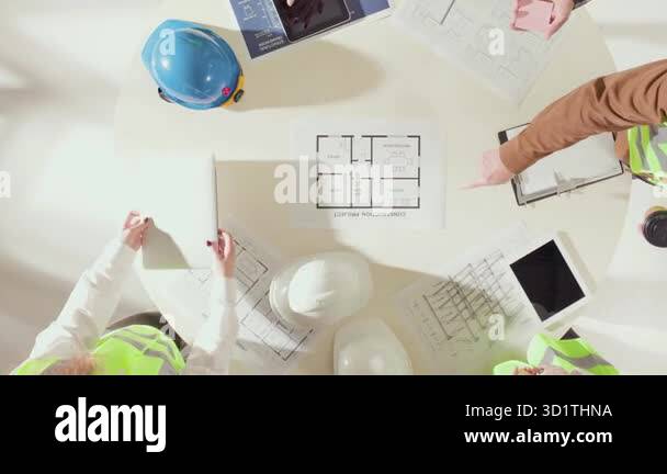Overhead view of engineers reviewing blueprints with digital tablets ...