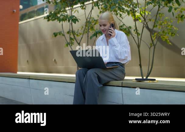 Professional woman sitting on bench outside, talking on smartphone and ...