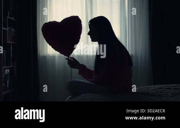 Silhouette of a sad and depressed woman sitting alone in a dark room ...