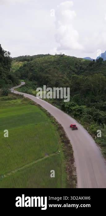 Drone view of a red buggy driving on a winding road through rice fields ...