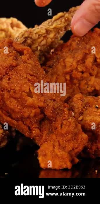 A hand reaches in to pick up assorted crispy fried chicken wings, drumsticks, and nuggets under ...