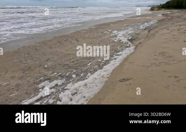 Foamy waves crash onto a sandy beach, illustrating the aftermath of ...