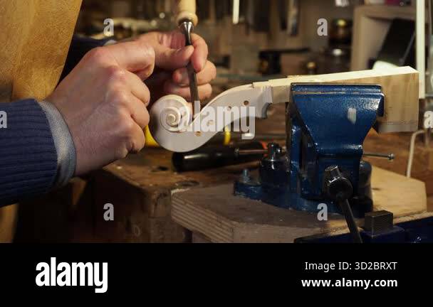 A master luthier uses a chisel to shape the delicate scroll of a violin ...
