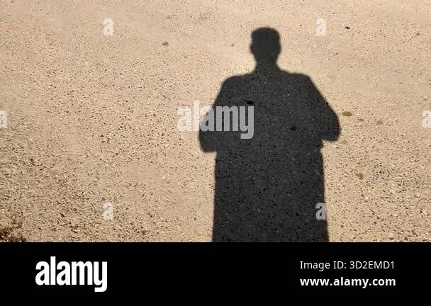 Man standing under bright sunlight as his moving clothes and shadow ...
