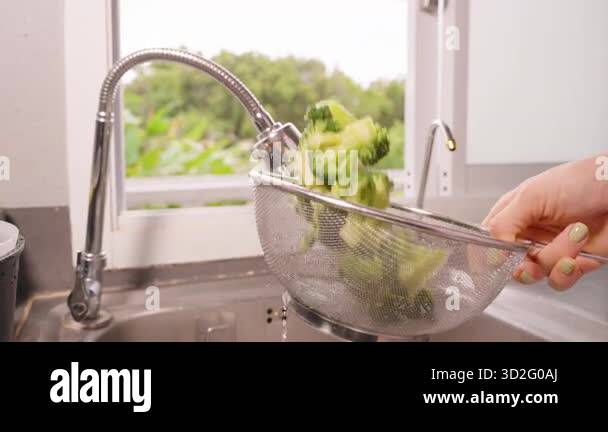 Hand Tossing Broccoli in Metal Strainer Above Sink in Slow Motion to ...