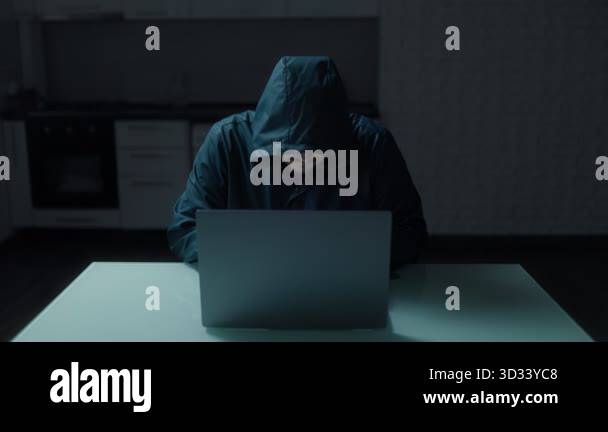 Close-up of an unidentifiable hacker with a hooded sweatshirt, working ...
