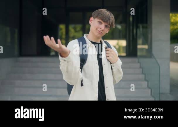 Playful teen student outdoors wearing a backpack, tilting his head with ...