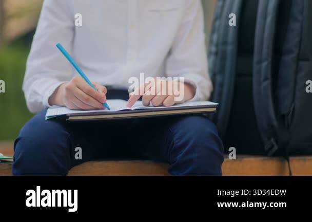 Close-up of a student writing in a notebook with a blue pen while ...