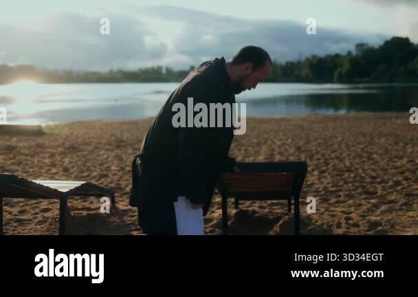 A man stands alone on a deserted beach, reading a letter with a serious ...
