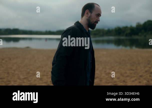 An emotional man stands alone on a sandy beach, clutching a letter and ...