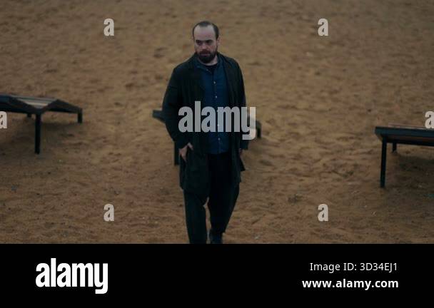 An agitated man in dark clothing walks alone on an empty beach. His ...