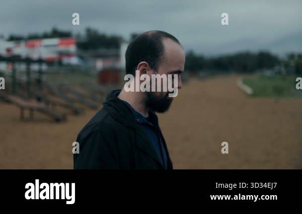 A deeply distressed man stands alone on a beach near a calm lake ...