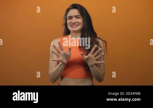 Hispanic young woman with long hair in an orange top raises open hands ...