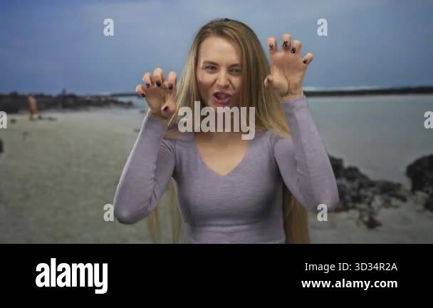 Woman playfully posing with claws in the air on a sunny beach with blue ...