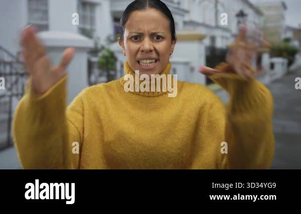 Woman yelling with hands on head wearing yellow sweater on street ...