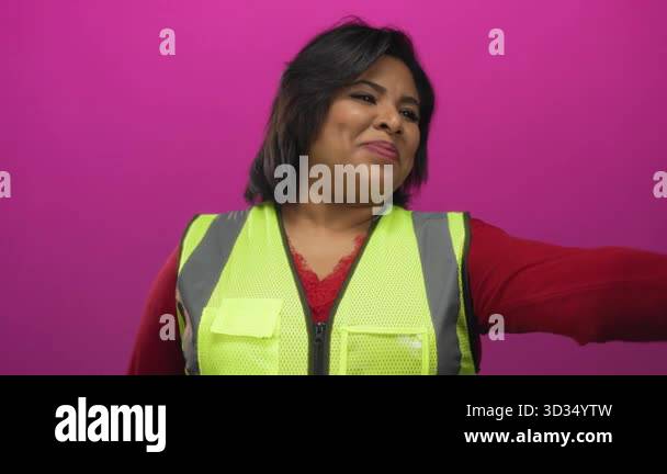 Plus size hispanic woman in reflective vest smiles against bright pink ...