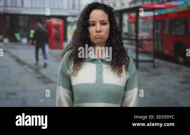 Woman standing outdoors with a sad expression near a red telephone ...