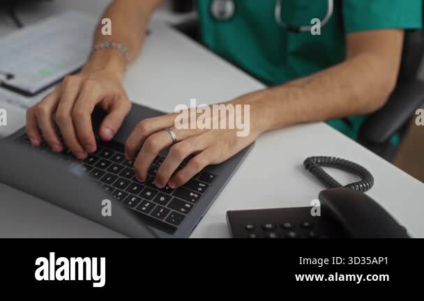 Young male doctor in green scrubs and stethoscope working on a laptop ...