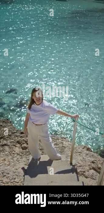 Woman smiling on steps at cala llombars with clear mediterranean waters ...