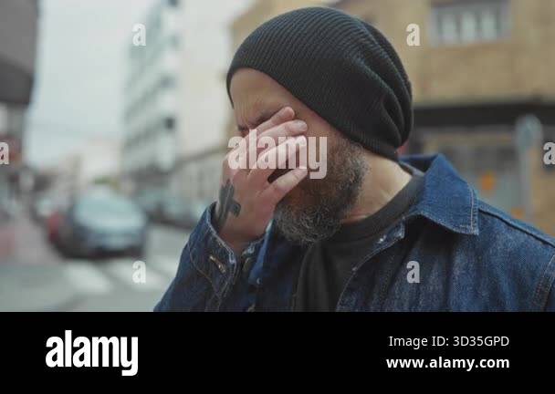 Bald bearded man outdoors in urban city street with hand on face ...