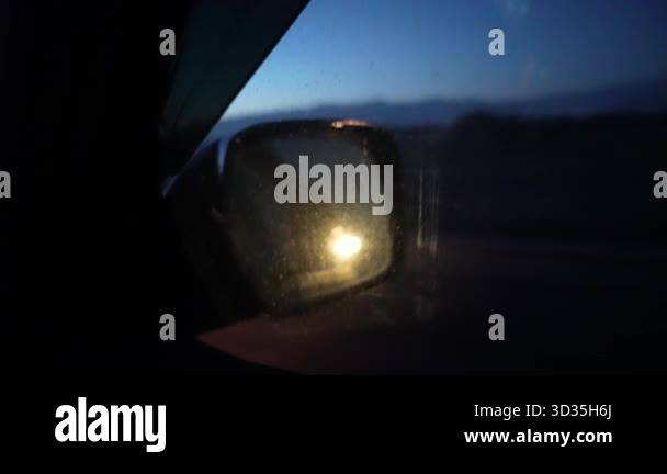 Reflection of vehicle headlights is captured in a side mirror during a ...