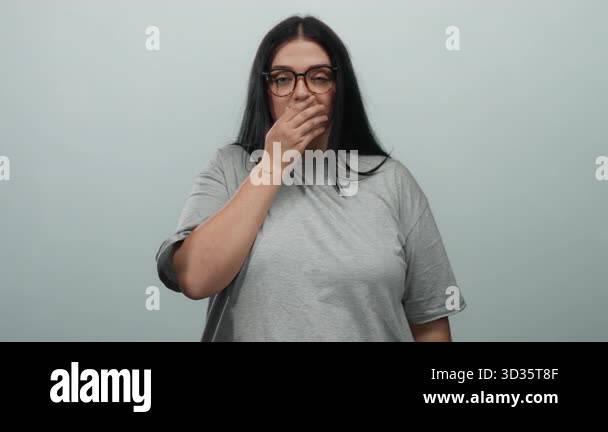 Woman with glasses covers mouth in shock on isolated white background ...
