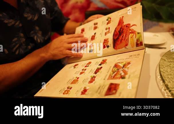 A person examines a menu in a warmly lit restaurant, focusing on ...