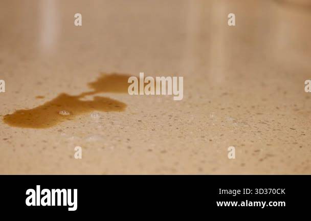 A hand wipes a coffee spill on a countertop using a cloth, under warm ...